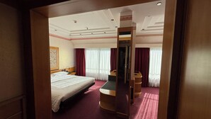 Quarto de hotel com uma cama grande, uma escrivaninha, um espelho e um guarda-roupa.