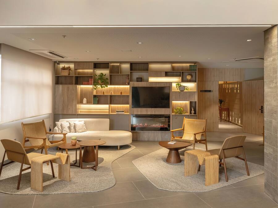 Uma sala de estar moderna com sofá, cadeiras, mesa de centro e televisão. Estantes com plantas e objetos decorativos.