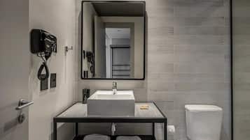 Uma casa de banho moderna com um espelho grande, uma pia, uma sanita e um secador de cabelo na parede.