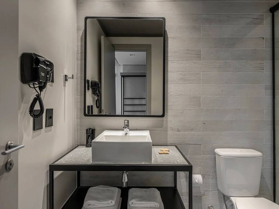 Uma casa de banho moderna com um espelho grande, uma pia, uma sanita e um secador de cabelo na parede.