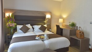Quarto de hotel com uma cama grande, mesas de cabeceira, uma escrivaninha e uma bandeja com itens de café da manhã.