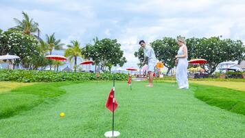 Um campo de golfe bem cuidado, com grama verde exuberante, putting green e bandeiras vermelhas marcando o buraco.