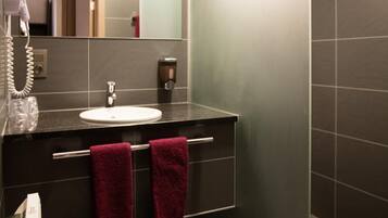 Uma casa de banho moderna com bancada escura, lavatório branco, espelho e secador de cabelo.
