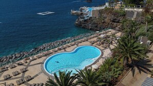 Área da piscina com espreguiçadeiras e vista para o oceano.