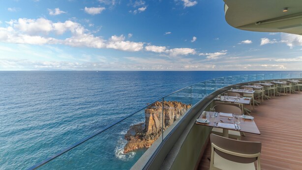 Um terraço com mesas e cadeiras com vista para o oceano e uma costa rochosa.