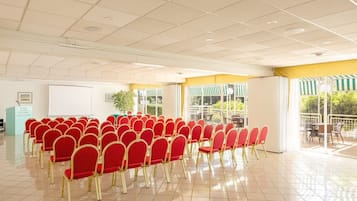 Uma sala de conferências com fileiras de cadeiras vermelhas e um quadro branco, janelas amplas e uma área de varanda.