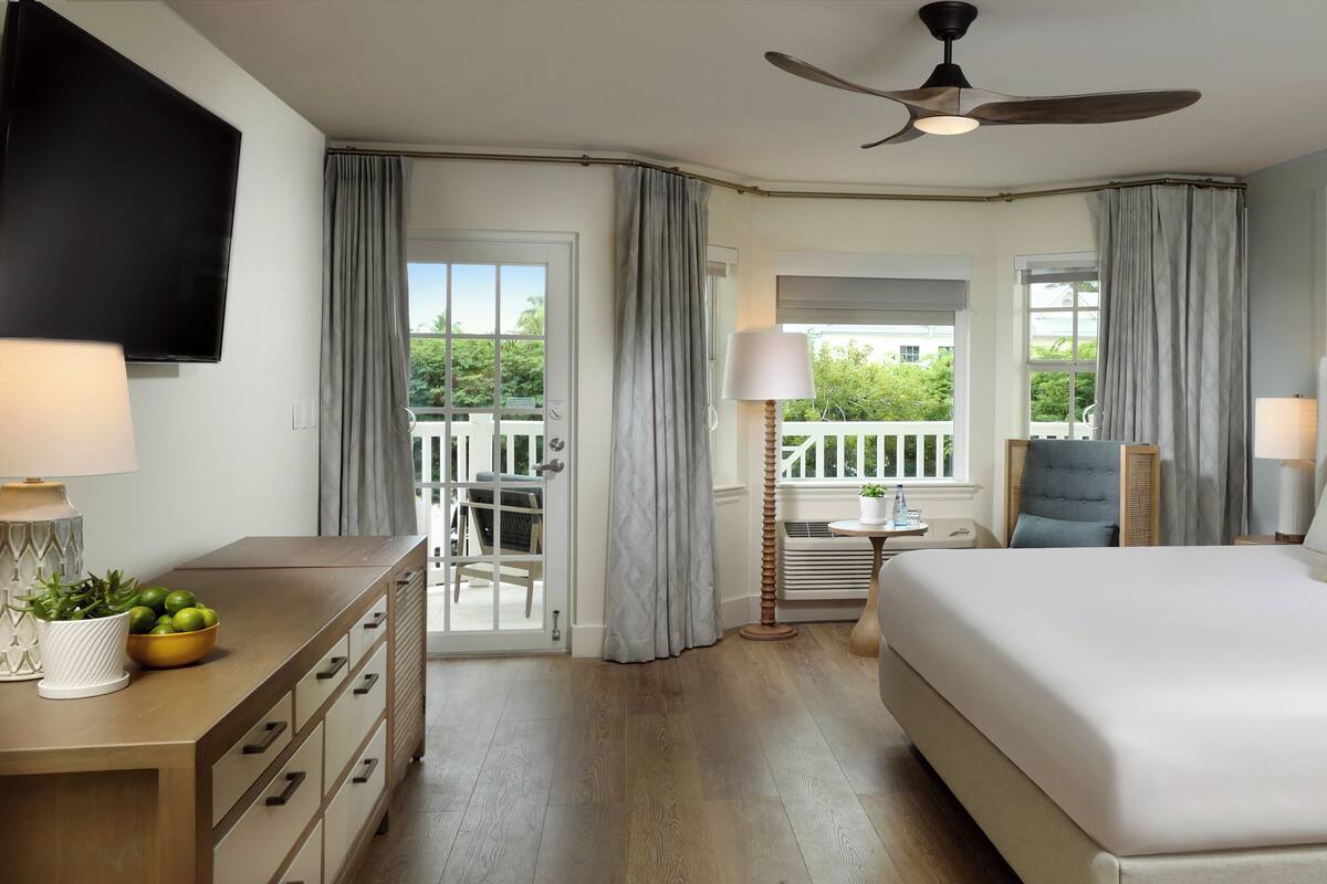Quarto de hotel com cama, escrivaninha, cadeira, varanda e ventilador de teto.