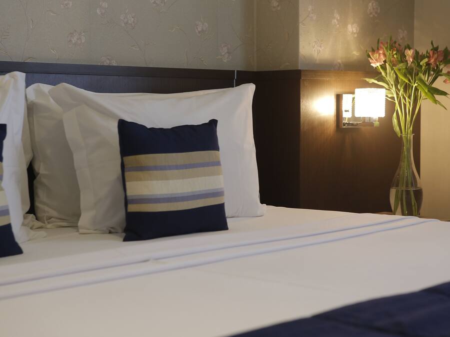 Cama bem arrumada com almofadas listradas, um vaso com flores e uma luminária na parede.