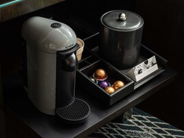 Uma máquina de café, um recipiente com cápsulas de café e um bule sobre uma bancada.