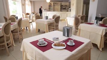 Uma sala de jantar com mesas preparadas para o café da manhã, incluindo croissants e café, e uma área de bar com garrafas.