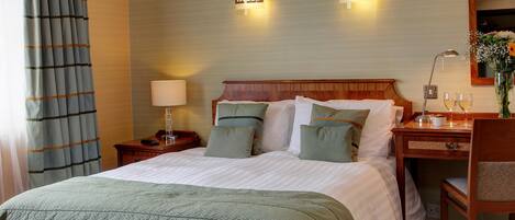 Quarto de hotel com uma cama grande, mesas de cabeceira, uma escrivaninha e uma cadeira. Há duas luminárias na parede e um espelho sobre a escrivaninha.