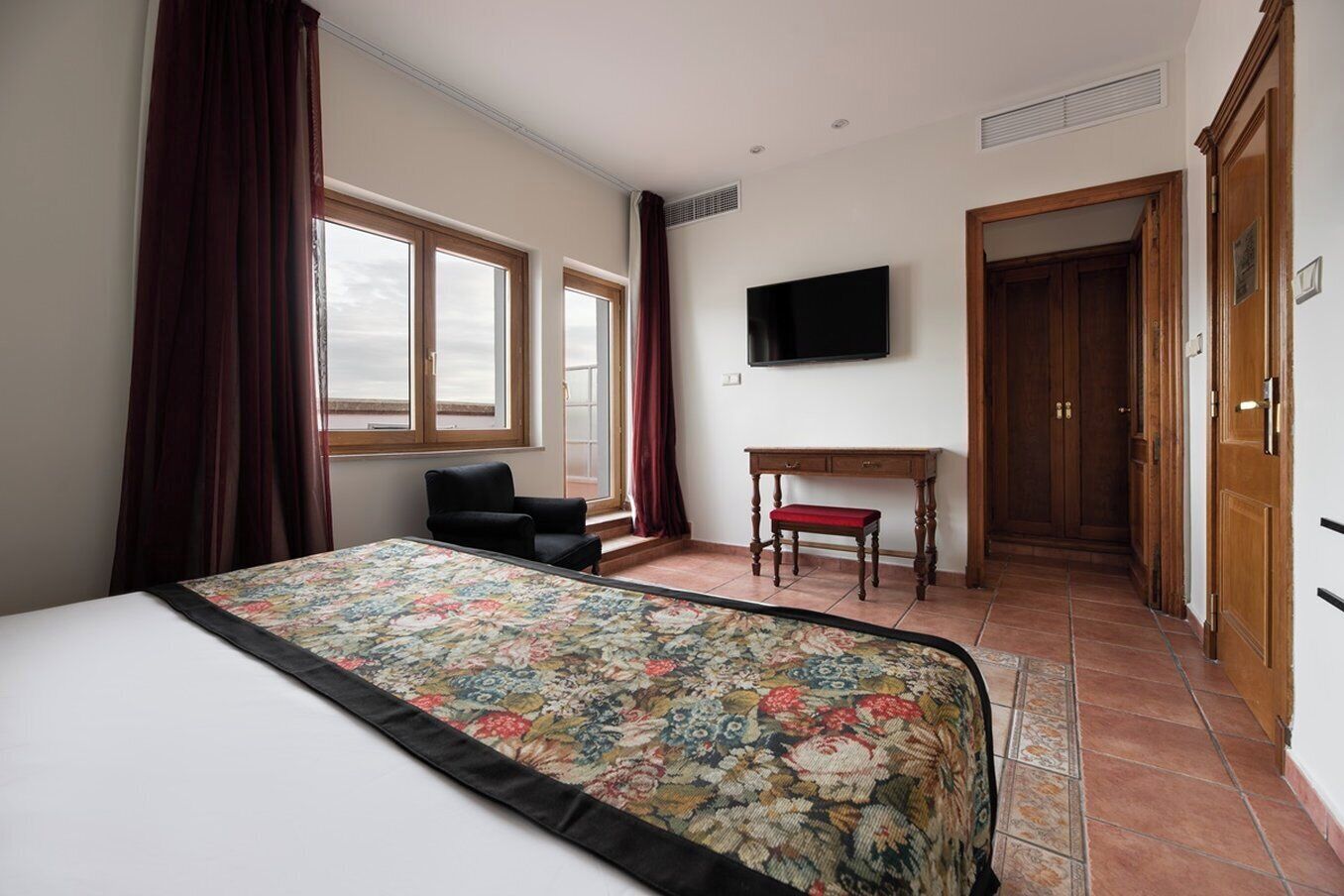 Quarto com uma cama, uma cadeira, uma escrivaninha, uma televisão e uma porta.