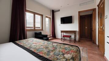Quarto com uma cama, uma cadeira, uma escrivaninha, uma televisão e uma porta.