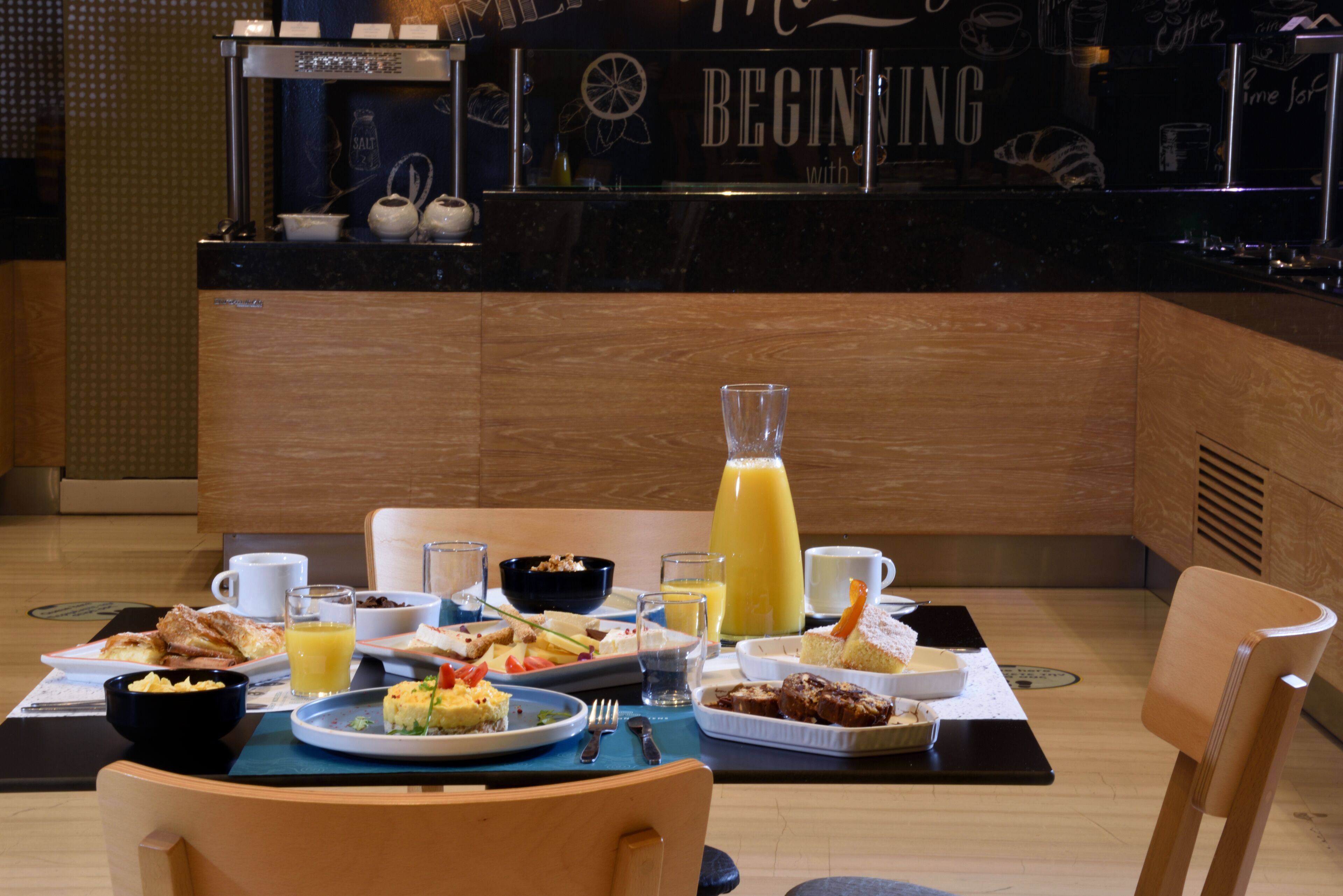 Mesa de café da manhã com diversos pratos, incluindo doces, frutas e um copo de suco de laranja.