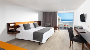 Quarto de hotel com cama, escrivaninha, cadeira, mesa pequena e varanda com vista para o mar.