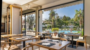 Restaurante com área externa e mesas voltadas para uma piscina e montanhas. As mesas estão montadas com talheres e guardanapos.