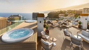 Terraço no telhado com hidromassagem, móveis de vime e vista para o mar e a paisagem urbana.