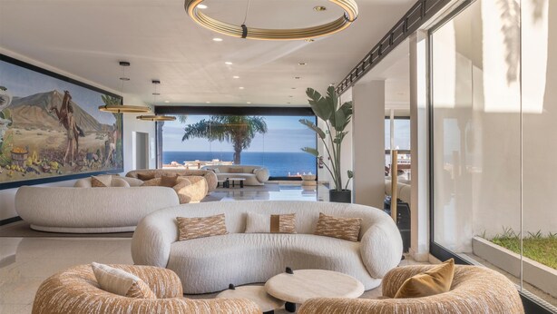 Uma sala de estar moderna com um sofá seccional grande, pufes redondos e vista para o mar.
