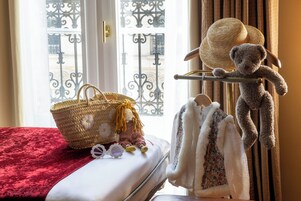 Uma cama com colcha vermelha, uma cesta de vime com um girassol, um urso de pelúcia e um chapéu de palha em um suporte.
