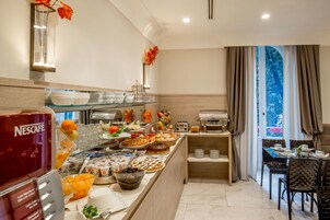 Uma área de buffet com uma máquina de café Nescafe, diversos alimentos e uma mesa de jantar com cadeiras.