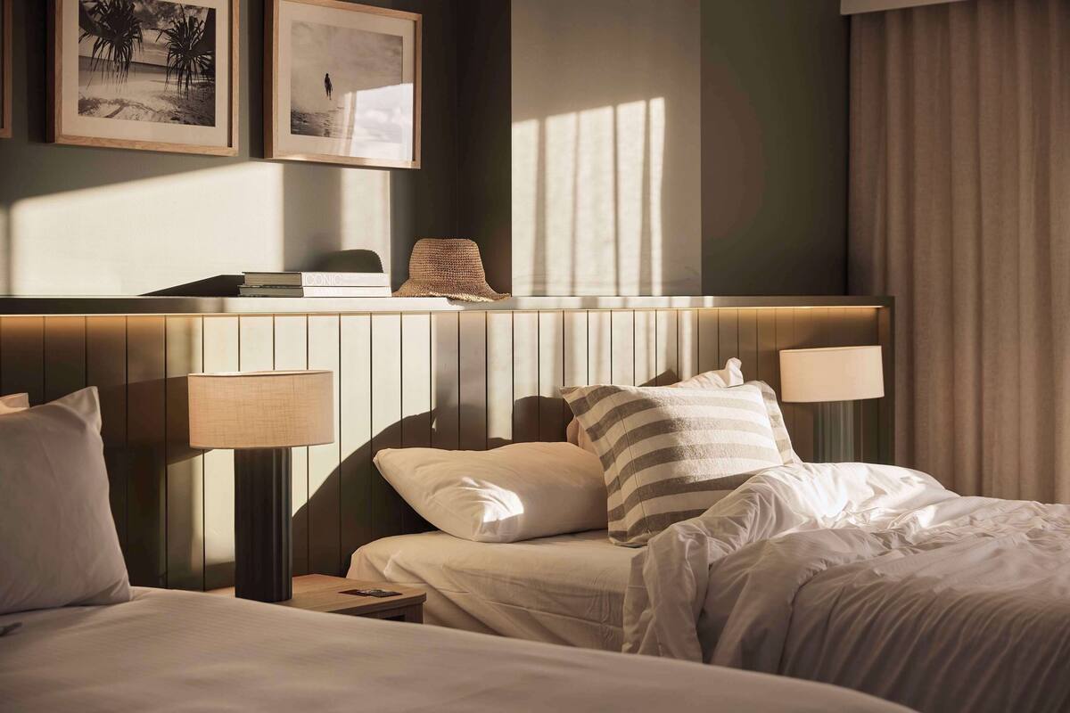 Quarto de hotel com uma cama, mesas de cabeceira, luminárias e quadros na parede.
