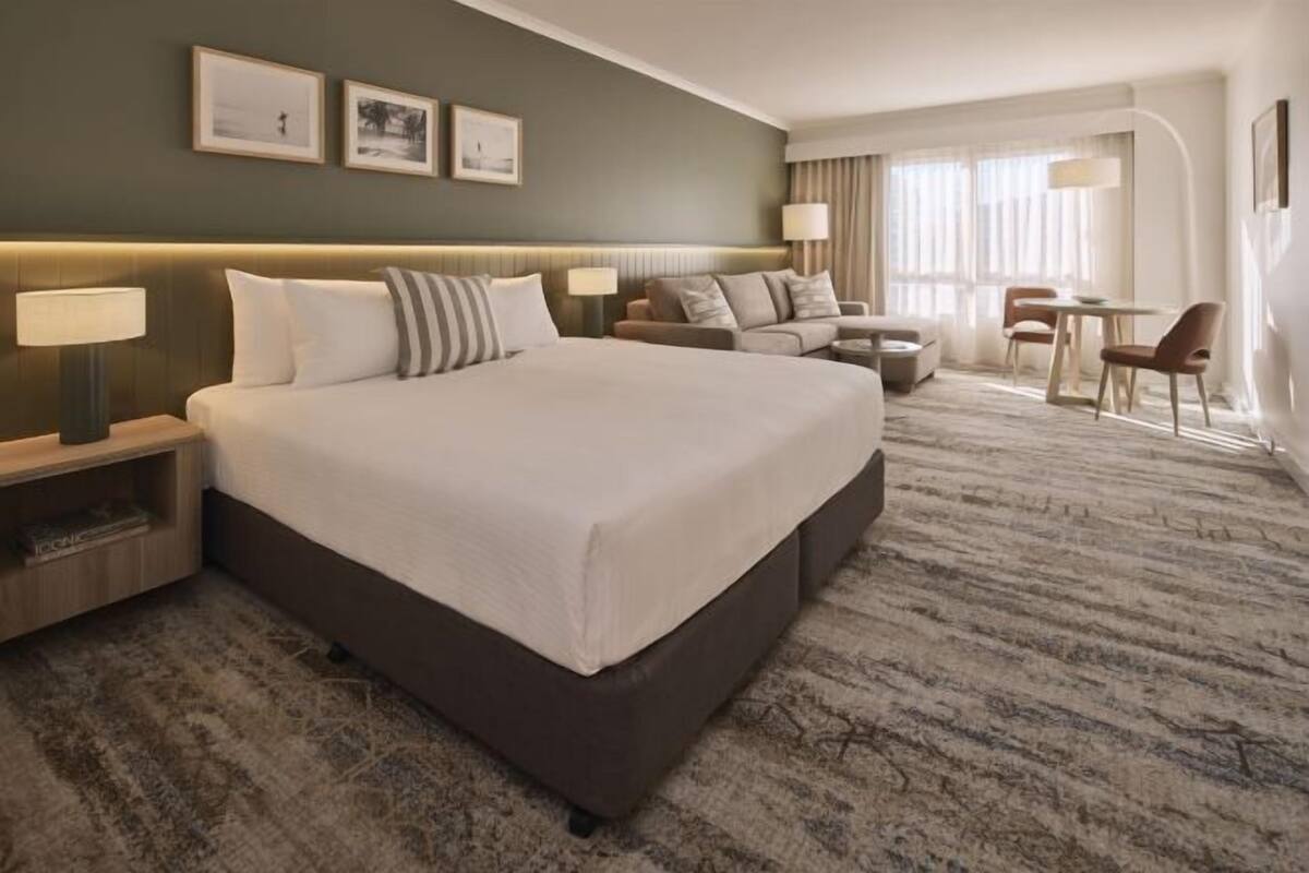 Quarto de hotel com uma cama grande, um sofá, uma escrivaninha e uma cadeira.