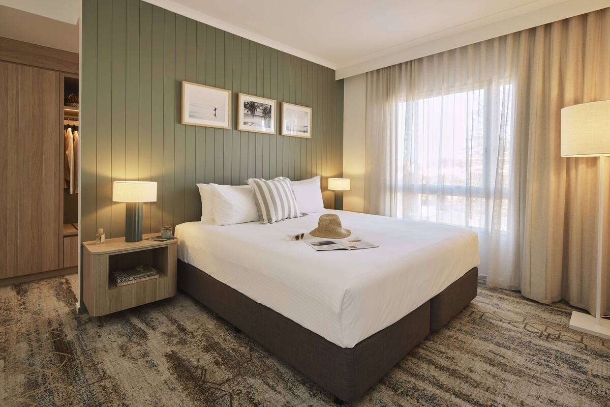 Quarto de hotel com cama grande, mesa de cabeceira, guarda-roupa e janela com cortinas.