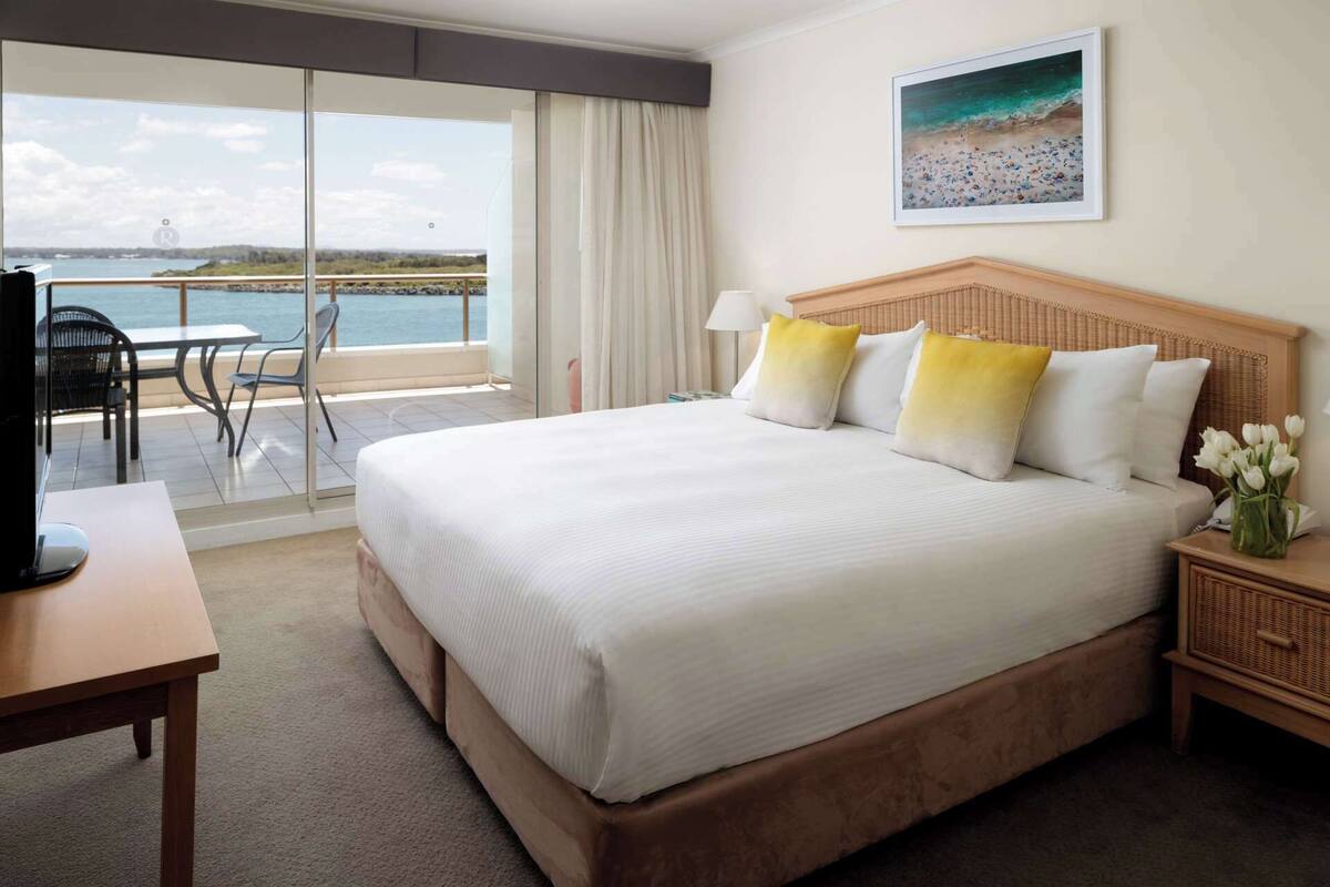 Quarto de hotel com uma cama grande, vista para o mar, espaço de refeições e um quadro na parede.