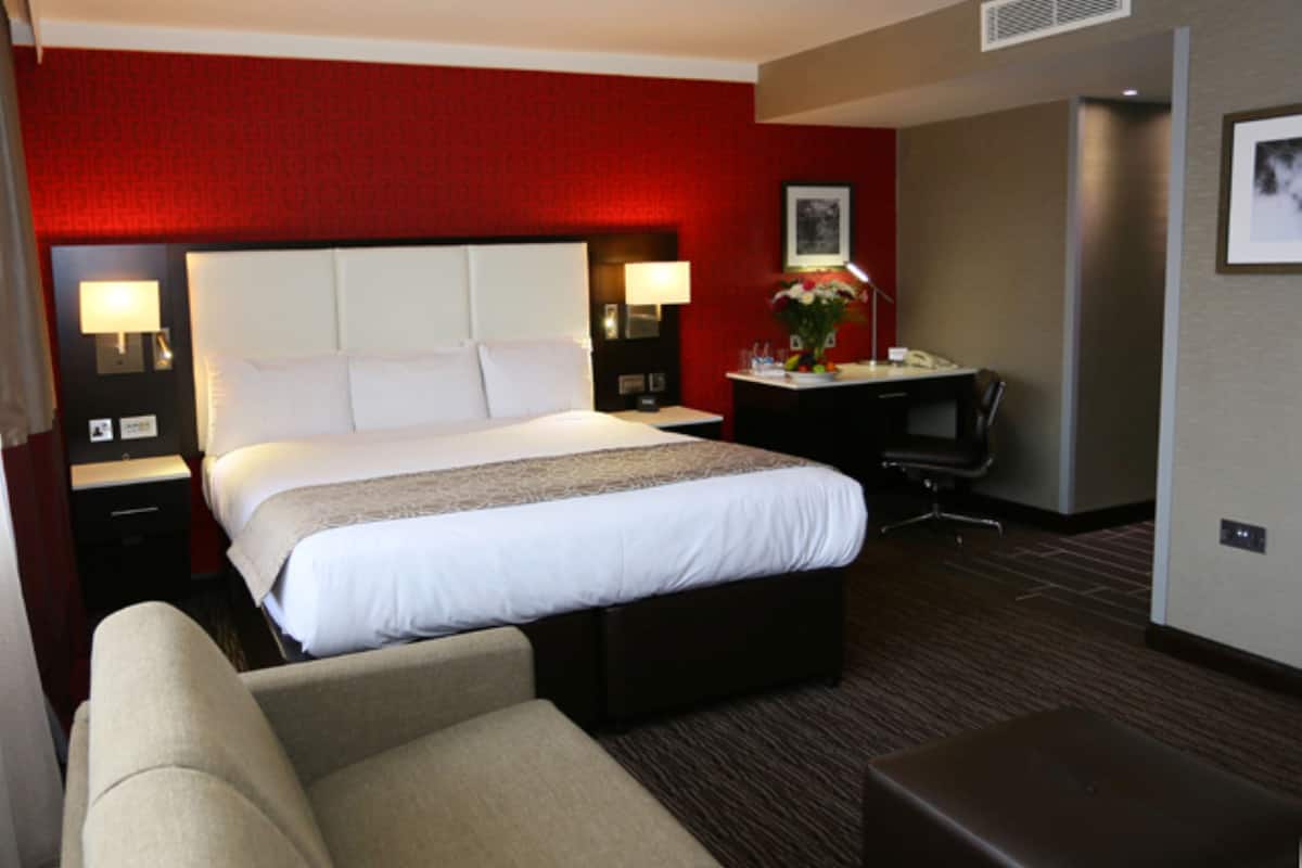 Quarto de hotel com uma cama grande, uma escrivaninha, uma cadeira e um pequeno sofá.