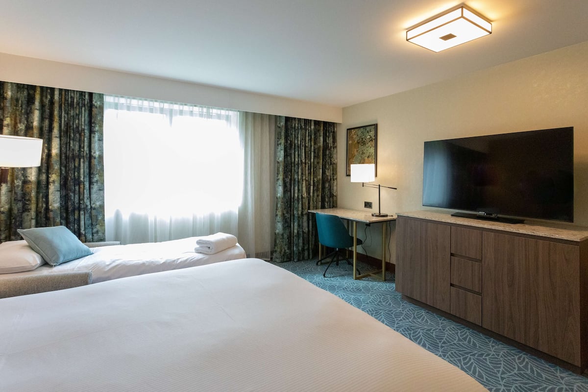 Quarto de hotel com uma cama grande, uma escrivaninha, televisão e uma janela com cortinas.