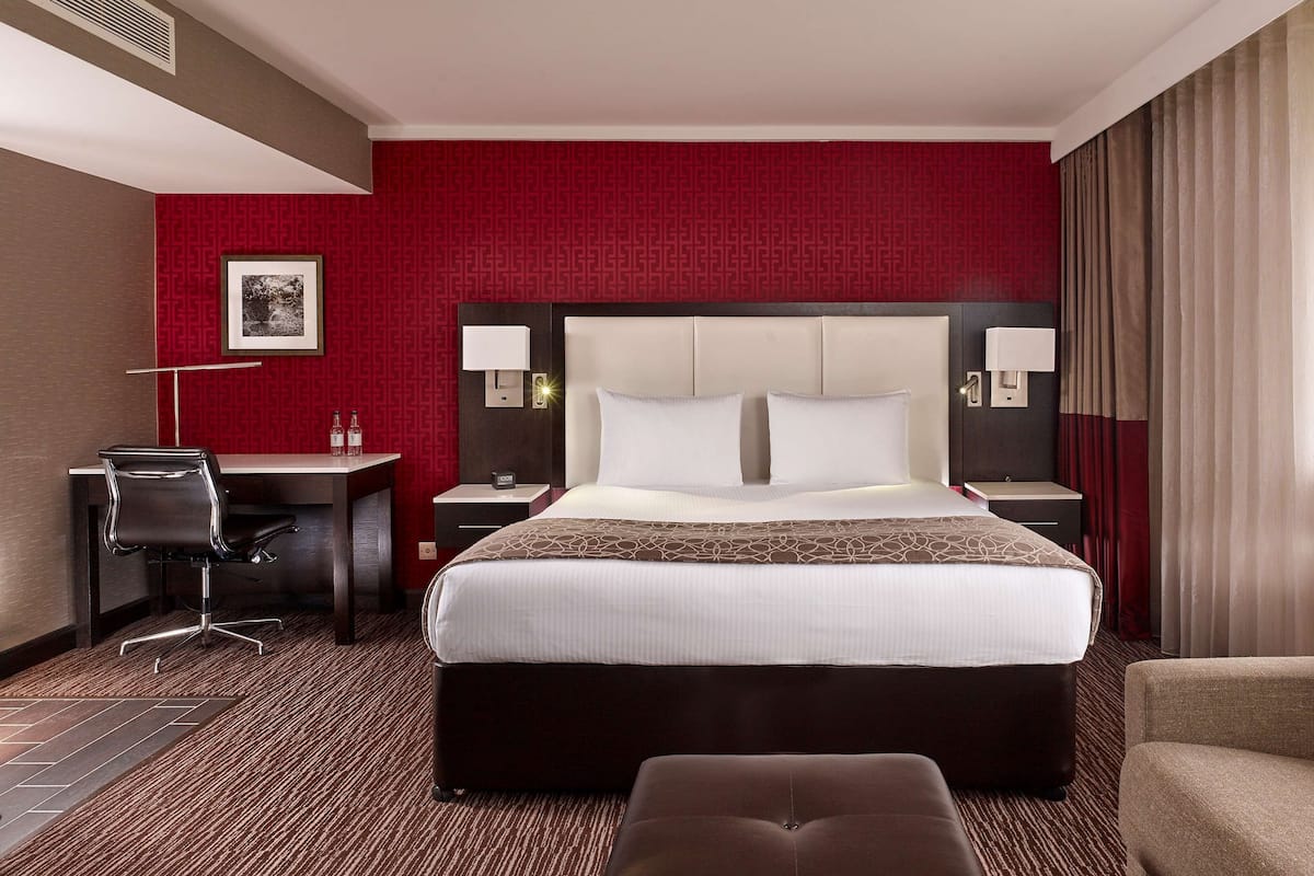 Quarto de hotel com cama grande, escrivaninha, cadeira e sofá.