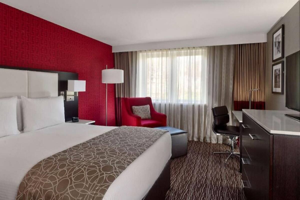 Quarto de hotel com uma cama grande, uma escrivaninha, uma cadeira, televisão e janela com cortinas.