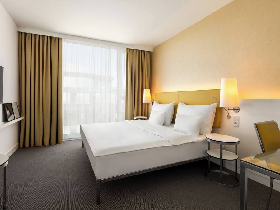 Quarto de hotel moderno com uma cama grande, uma escrivaninha, uma cadeira e uma televisão.