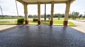 Um espaço ao ar livre coberto, com piso de tijolos, colunas e um banco.