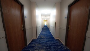 Um corredor de hotel com portas de madeira, carpete azul e um candeeiro no teto.