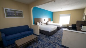Quarto de hotel com sofá azul, duas camas, uma escrivaninha e uma janela grande.