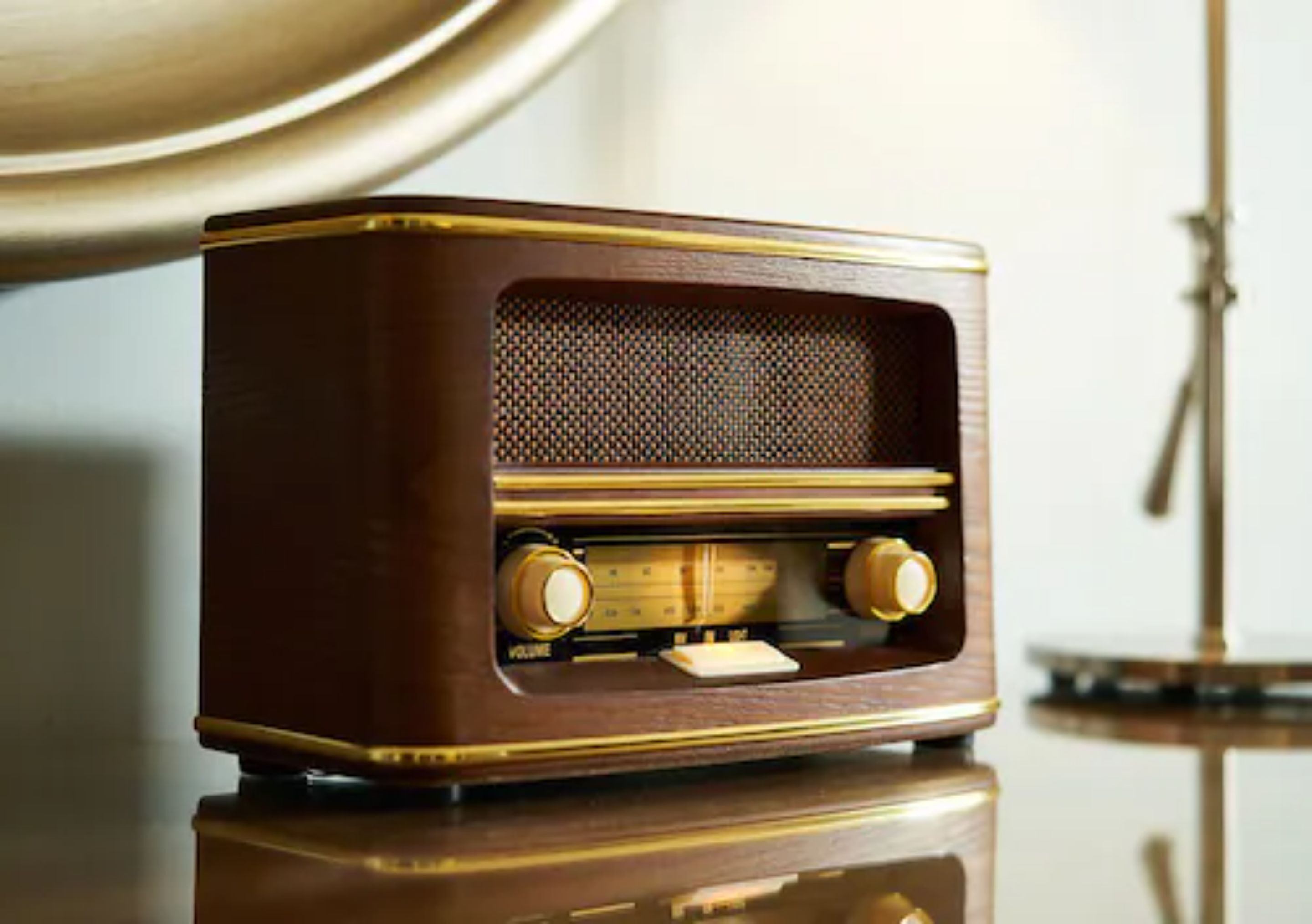 Rádio antigo com acabamento em madeira e detalhes dourados, apoiado em uma superfície refletora.