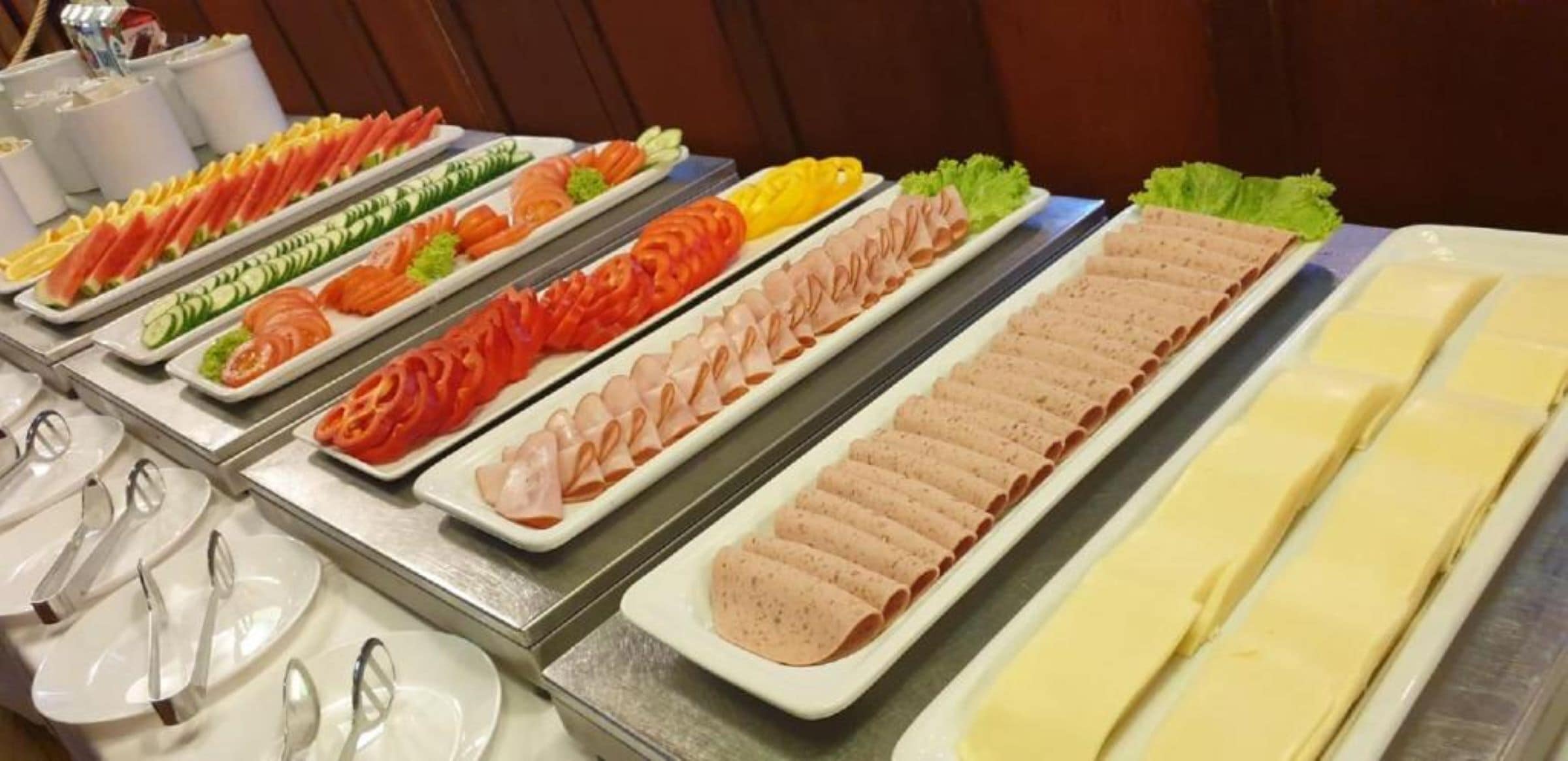 Buffet com diversos alimentos, incluindo carnes fatiadas, legumes e queijos.