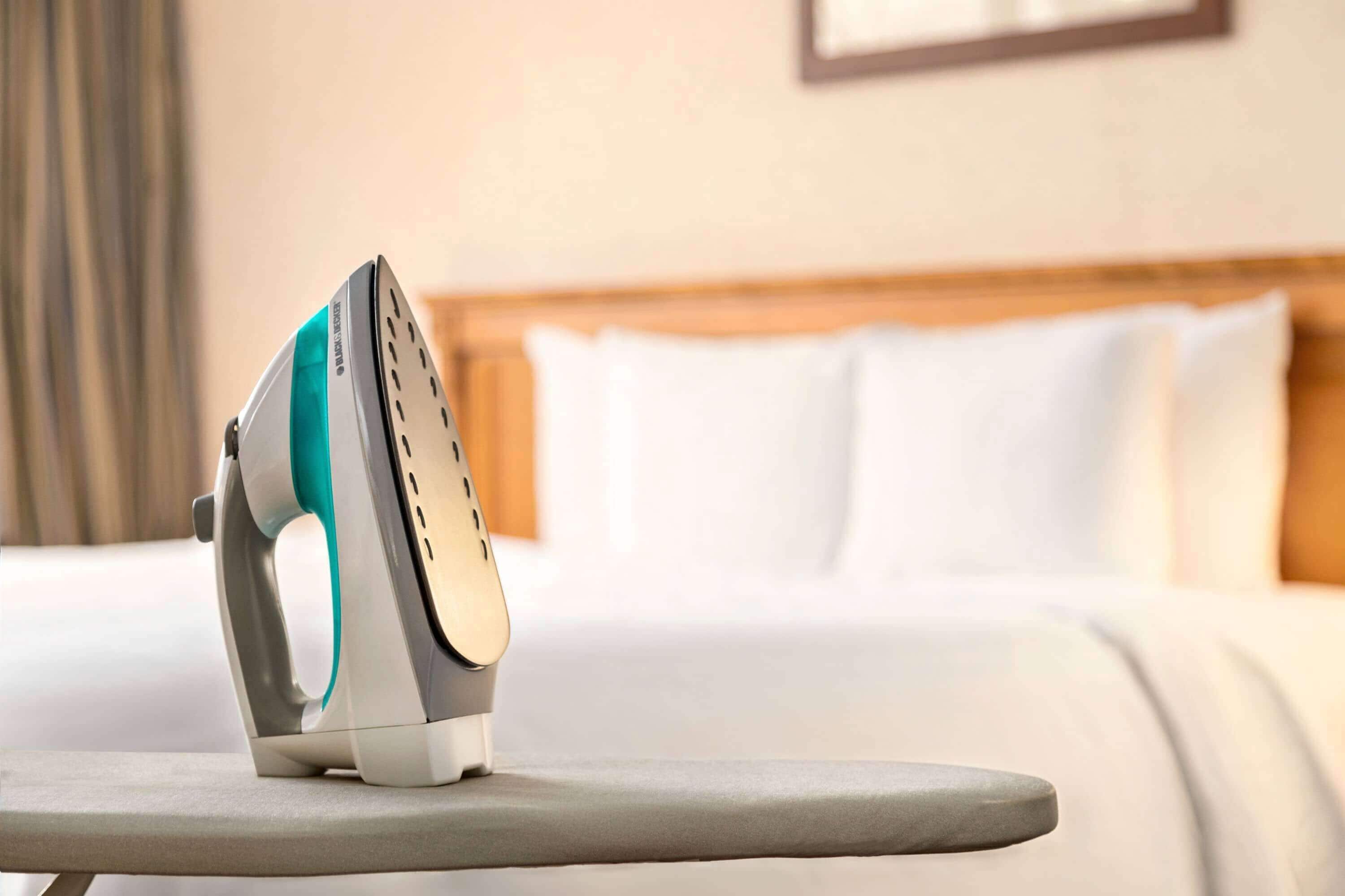 Quarto de hotel com uma cama, mesa de cabeceira e um centro de passar roupa fixado na parede.