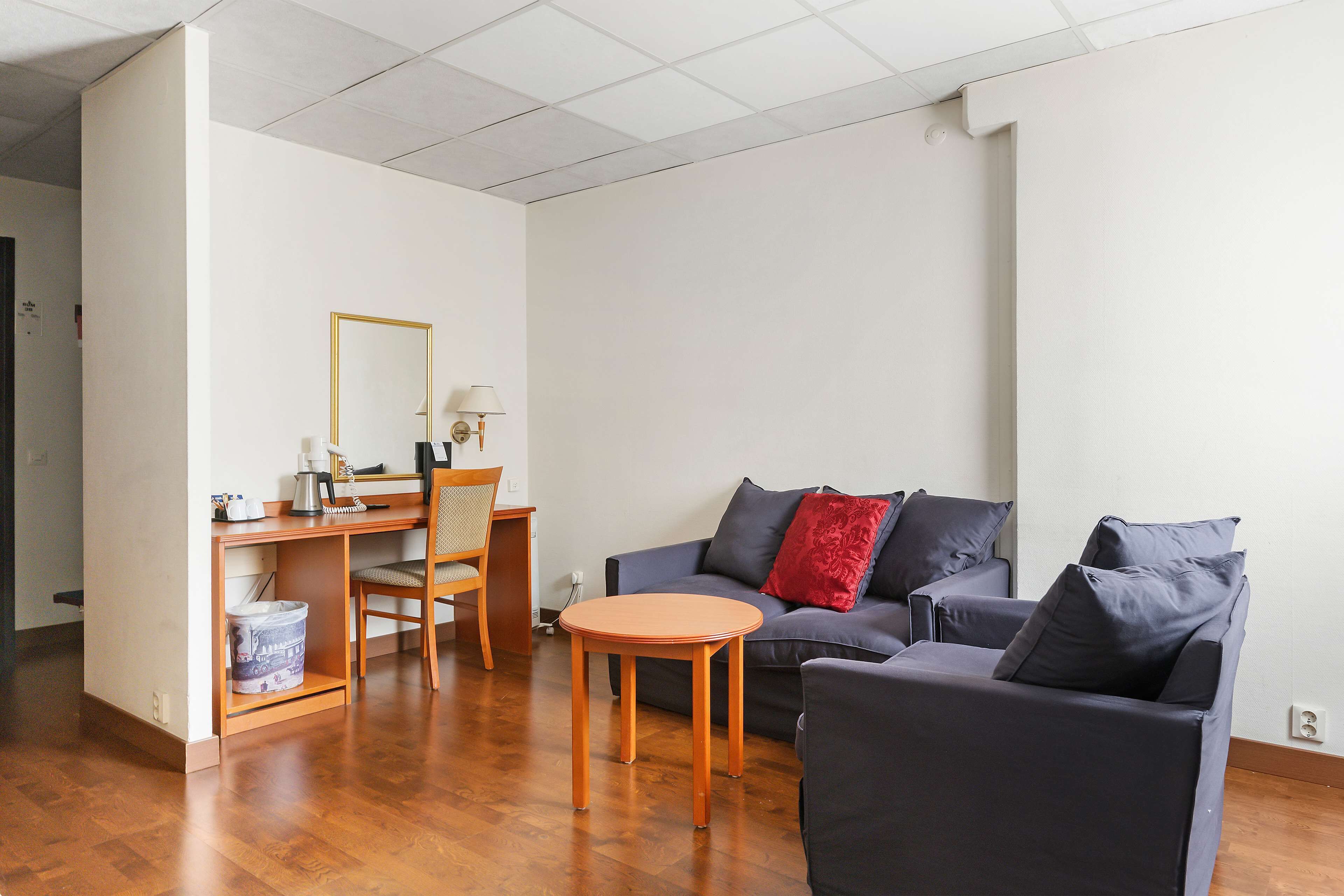 Uma sala de estar com sofá, uma mesinha, uma cadeira, escrivaninha e abajur.
