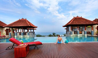 Uma área à beira da piscina com cadeiras de lounge vermelhas, um deck de madeira e vista para o oceano.