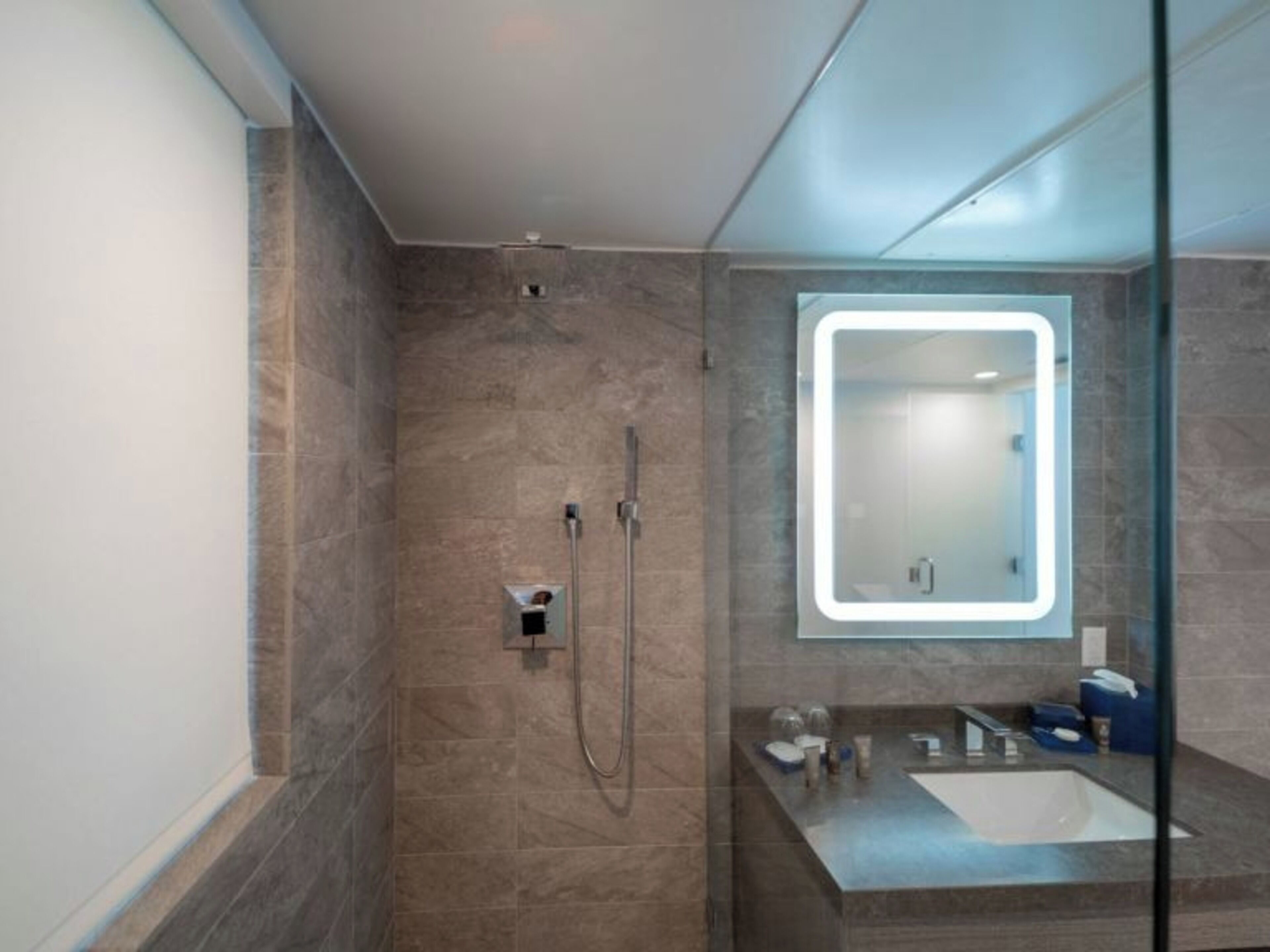 Uma casa de banho moderna com cabine de duche em vidro, lavatório embutido e espelho com iluminação embutida.