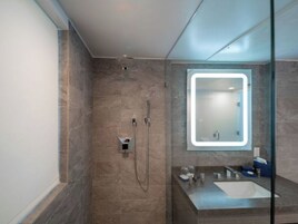 Uma casa de banho moderna com cabine de duche em vidro, lavatório embutido e espelho com iluminação embutida.