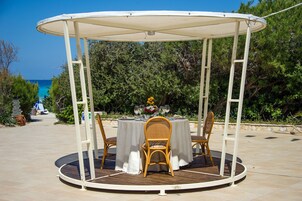 Uma área de refeições ao ar livre coberta, com uma mesa posta para dois, rodeada por cadeiras, com vista panorâmica.