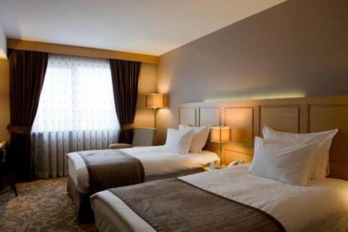 Quarto de hotel com duas camas, uma escrivaninha, uma cadeira e uma janela com cortinas.