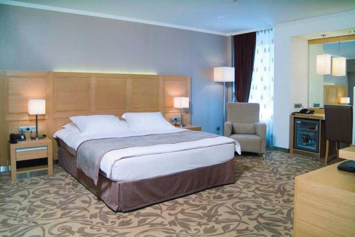 Quarto de hotel com uma cama grande, mesas de cabeceira, escrivaninha, cadeira e espelho.