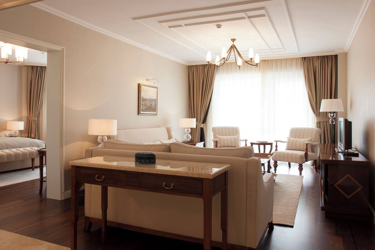 Quarto de hotel com cama, sofá, escrivaninha e cadeira. Há um candelabro e um quadro na parede.