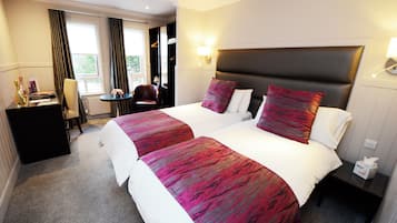 Quarto de hotel com duas camas, uma escrivaninha, uma cadeira e uma janela com cortinas.