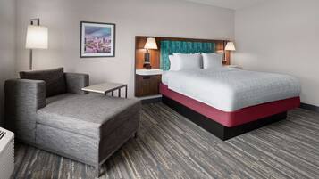 Quarto de hotel com cama, sofá, mesa de cabeceira, abajur e um quadro na parede.