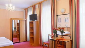 Quarto de hotel com cama, escrivaninha com cadeira, televisão, espelho e armário.
